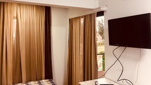 Quarto de hotel com cama, cortinas, televisão na parede e um relógio.