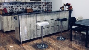 Uma cozinha moderna com bancada de mármore, dois bancos altos, uma mesa de jantar com cadeiras e um dispensador de água.