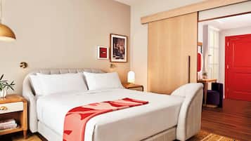 Quarto de hotel moderno com cama, mesa de cabeceira, abajur e uma porta vermelha.