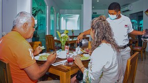 Ambiente de restaurante com um garçom servindo comida aos hóspedes.