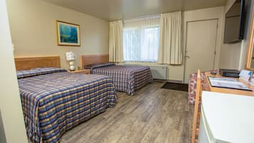 Quarto de hotel com duas camas, uma escrivaninha, uma televisão e uma janela com cortinas.