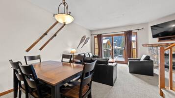 Uma sala de estar moderna com área de jantar, lareira e uma grande janela com vista para uma montanha.