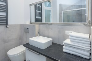 Casa de banho com lavatório branco, sanita e pilha de toalhas brancas.