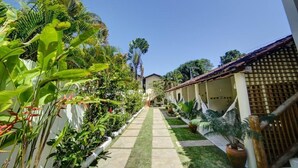Uma trilha leva a um edifício com telhado de cerâmica, cercado por vegetação exuberante e um céu azul límpido.