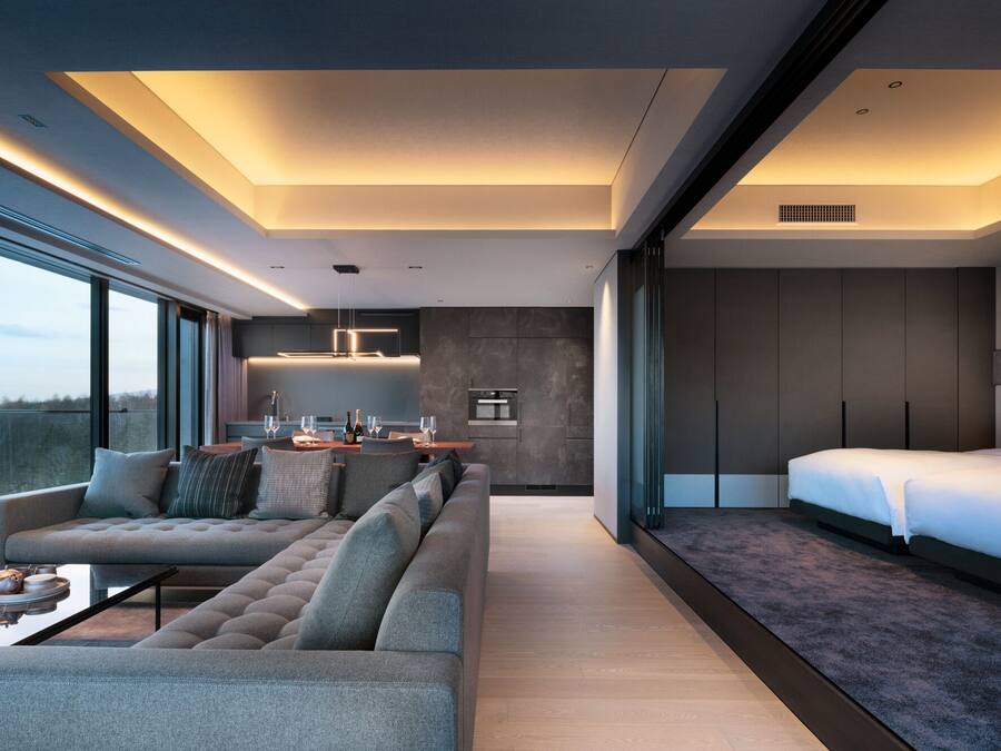 Quarto de hotel moderno com uma cama grande, um sofá, área de refeições e cozinha.