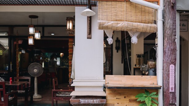 Interior acolhedor de café com mesas de madeira, um pilar de tijolos e um letreiro com a inscrição 'THANK YOU COFFEE'.