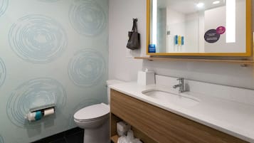 Um banheiro moderno com vaso sanitário, pia e espelho. Há um porta-toalhas com uma sacola pendurada e um suporte de papel higiênico na parede.