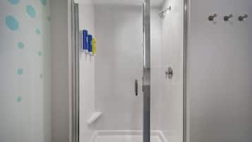 Divisória de chuveiro envidraçada com parede de azulejos brancos, chuveiro e prateleira com produtos de higiene pessoal.