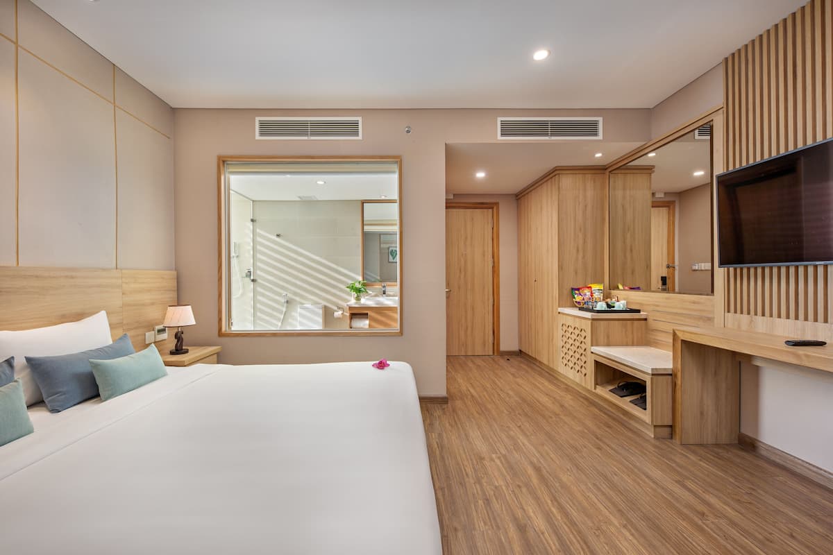 Quarto de hotel moderno com uma cama grande, um guarda-roupa de madeira, uma secretária com espelho e uma televisão.