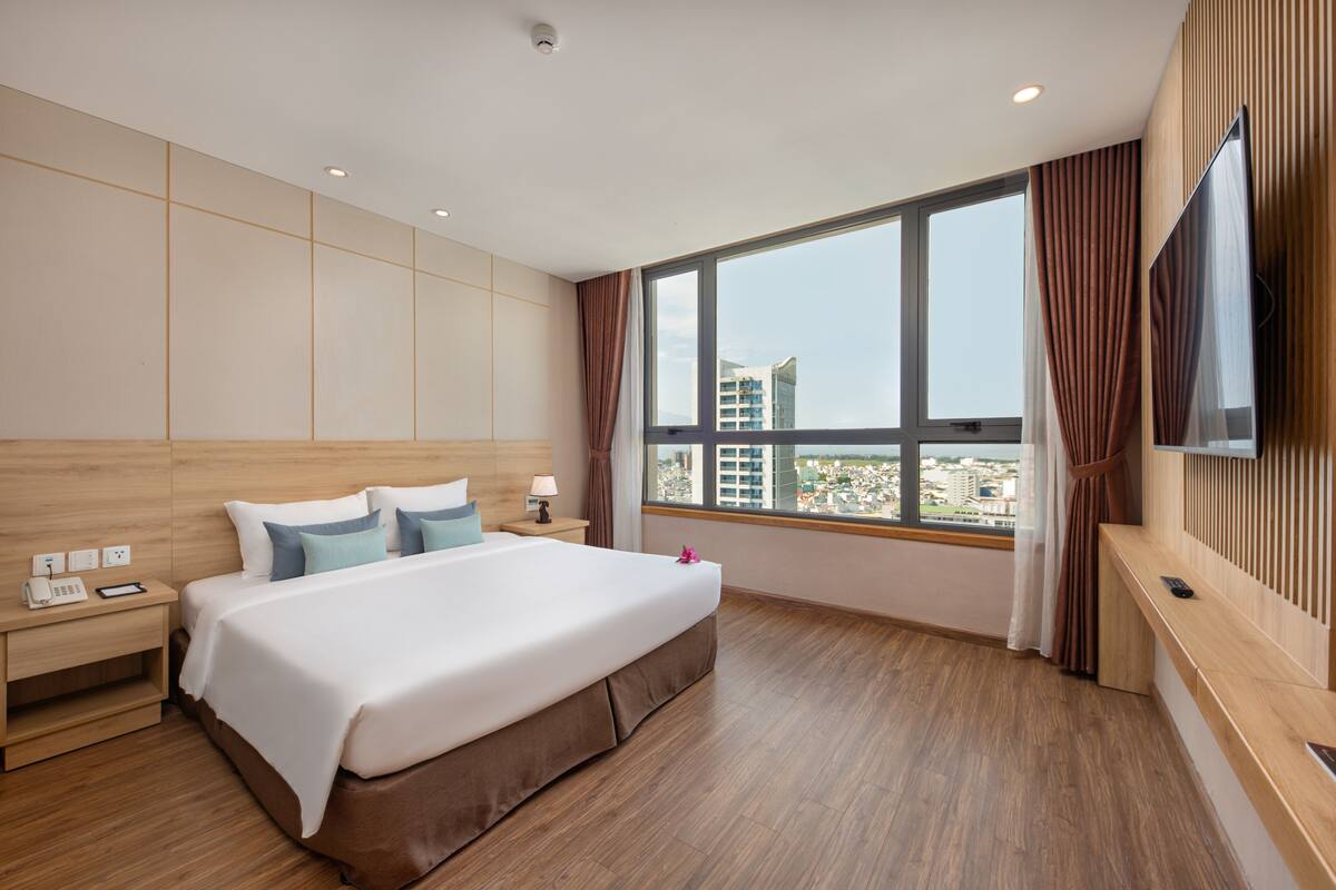 Quarto de hotel moderno com uma cama grande, painéis de parede de madeira, uma TV montada e uma janela ampla com cortinas.