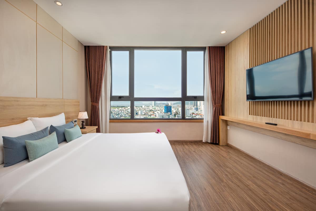 Quarto de hotel com uma cama grande, televisão na parede e janela com vista para a cidade.