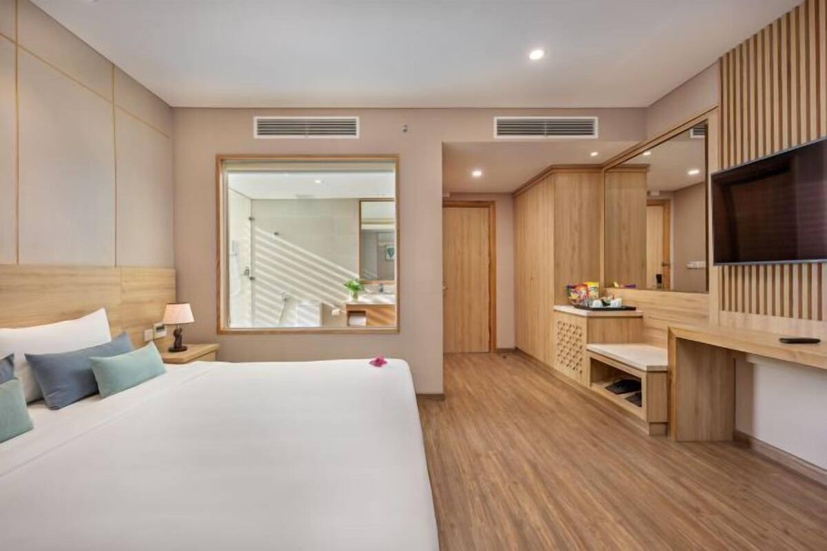 Quarto de hotel moderno com uma cama grande, televisão, guarda-roupa e secretária.