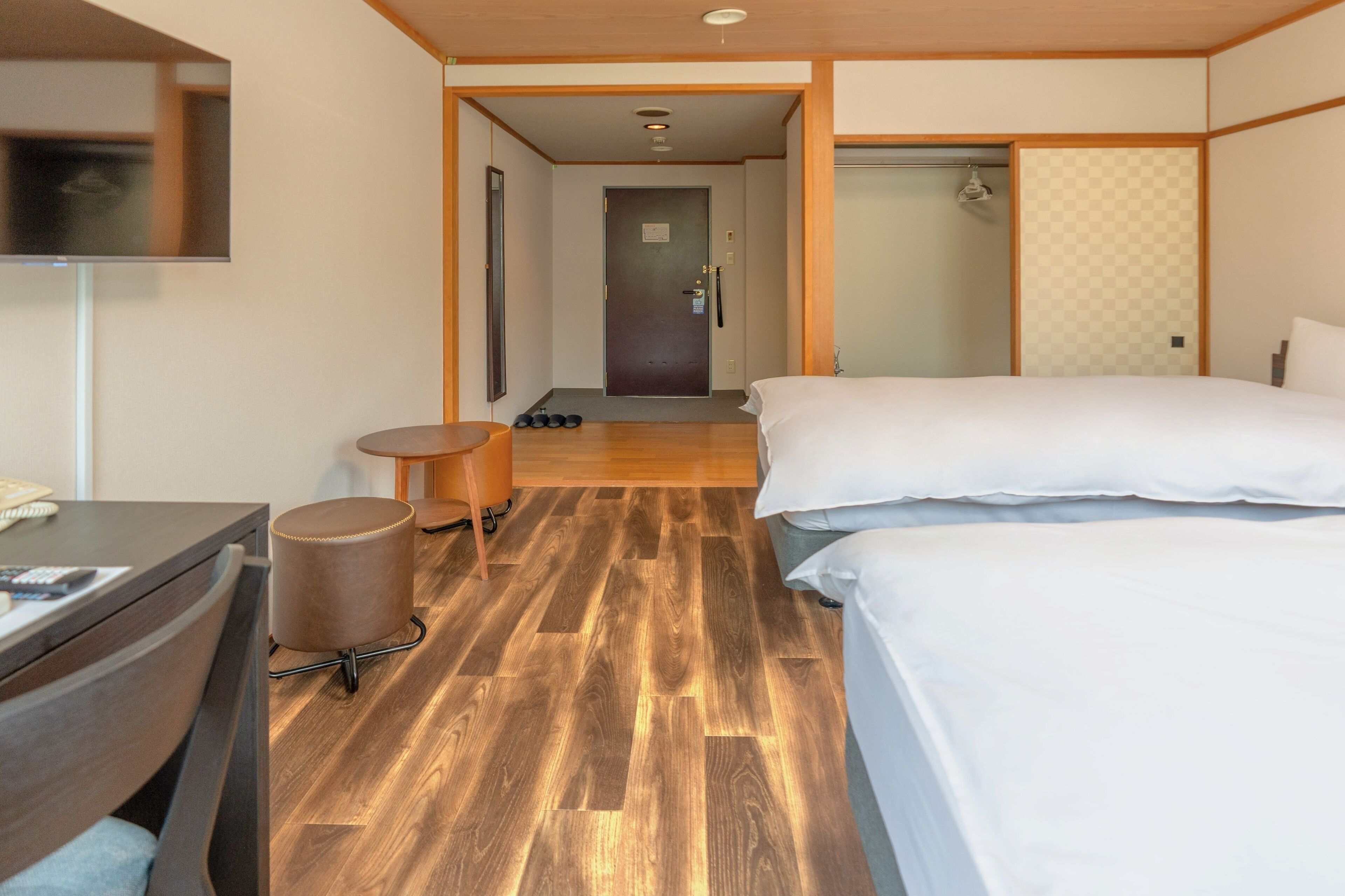 Quarto de hotel com piso de madeira, uma cama, uma escrivaninha e uma lixeira.