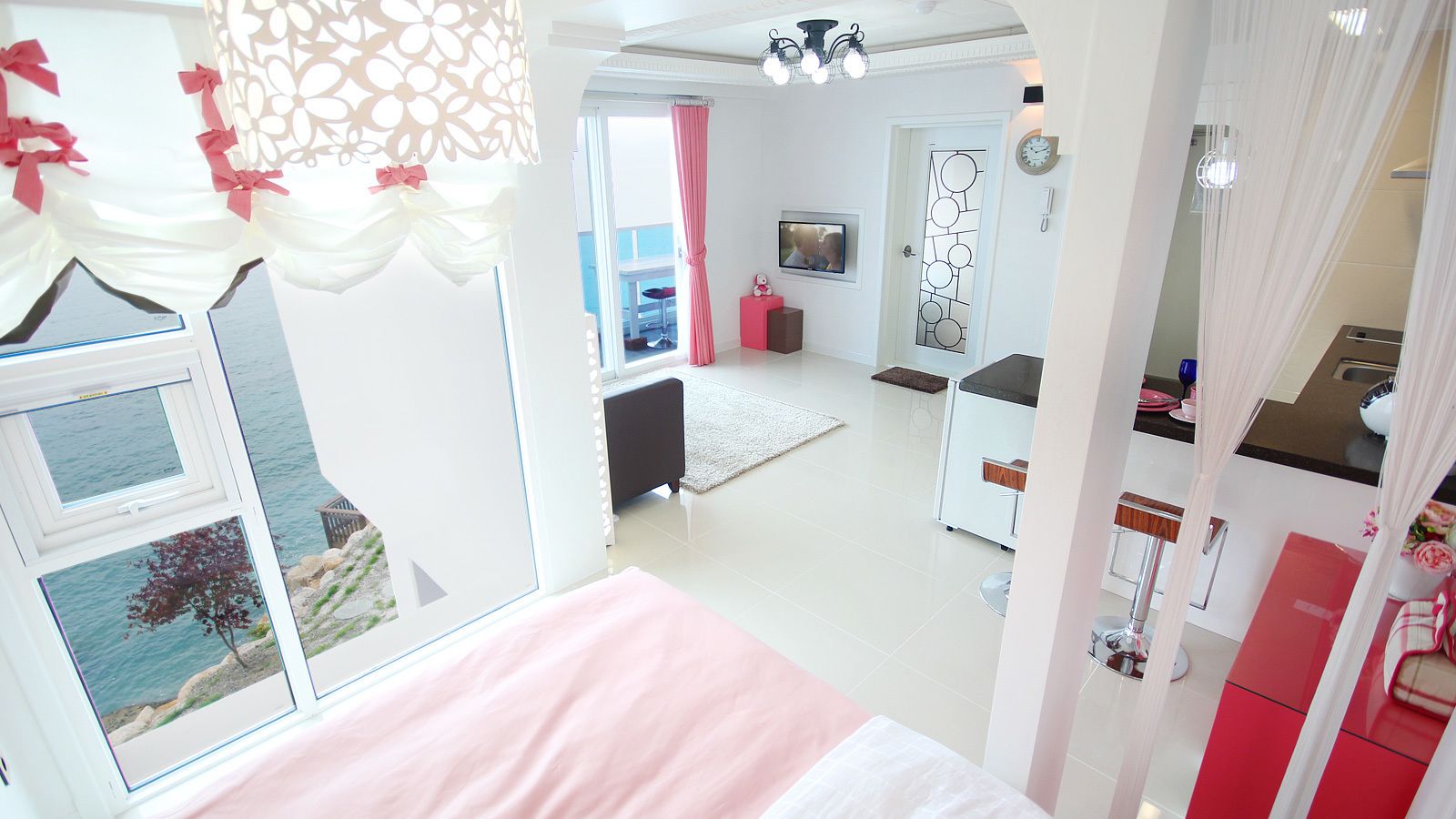 Quarto com vista para o mar, televisão, cozinha e banheiro.