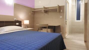 Quarto com cama, mesa de cabeceira, luminária, escrivaninha, cadeira e porta que dá para outro cômodo.