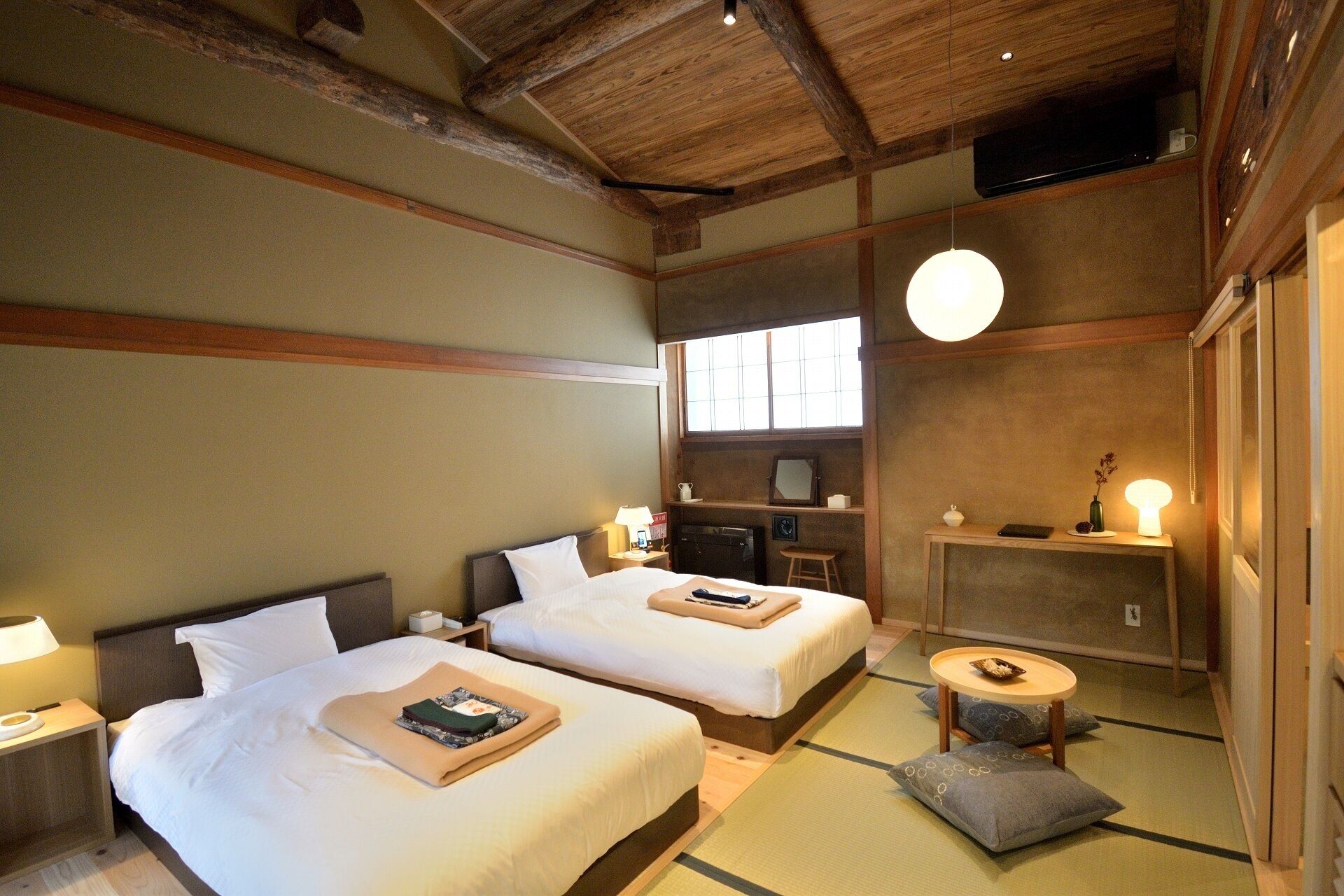 Quarto de hotel com duas camas, uma mesinha, uma televisão e uma janela.