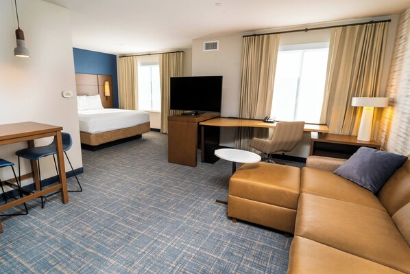 Quarto de hotel com cama, escrivaninha com televisão, sofá e uma pequena mesa.