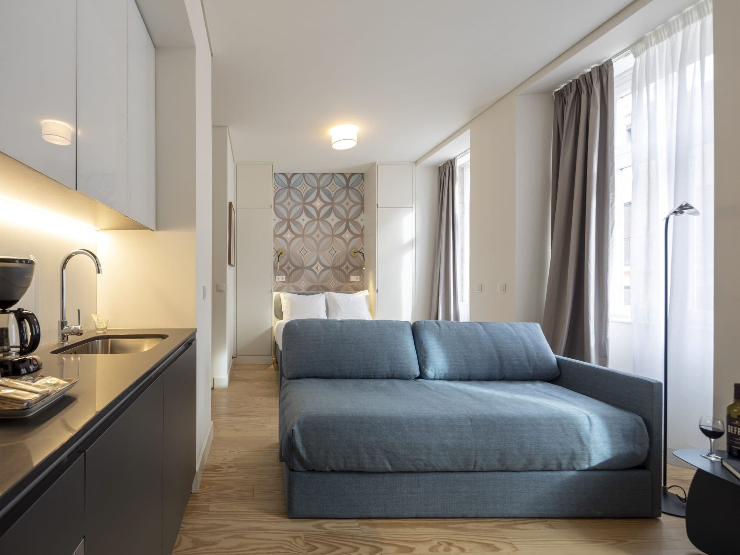 Quarto de hotel moderno com cozinha compacta, sofá, cama e vista para a cidade.