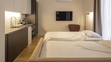 Quarto de hotel com cama, televisão, cozinha compacta e janela com cortinas.