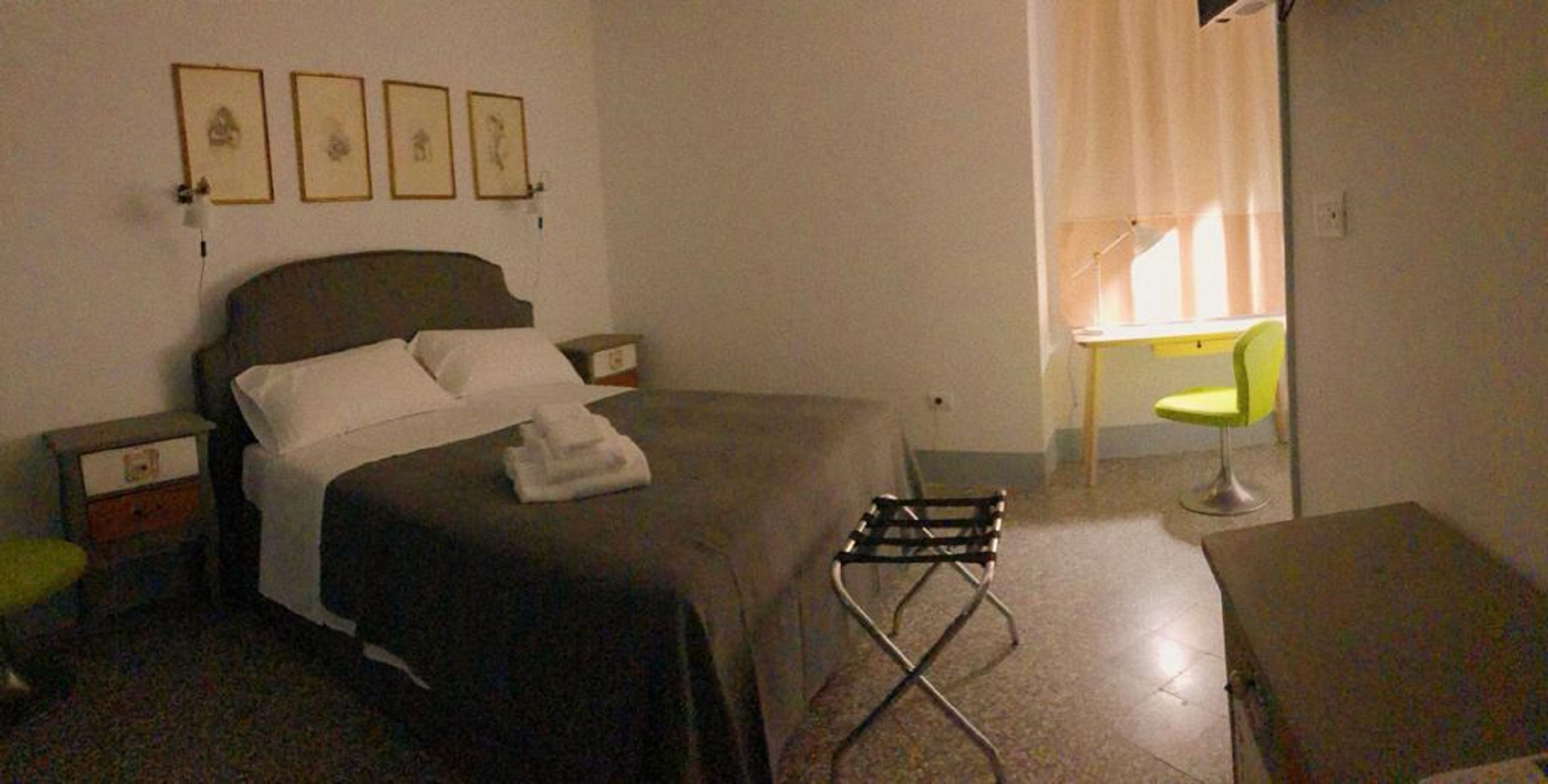 Quarto com cama, mesas de cabeceira, uma cadeira e janela com cortinas.