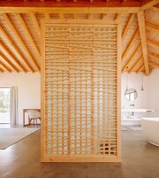 Quarto com teto e divisória em madeira, uma escrivaninha, uma cadeira, banheiro com banheira e luminária pendente.