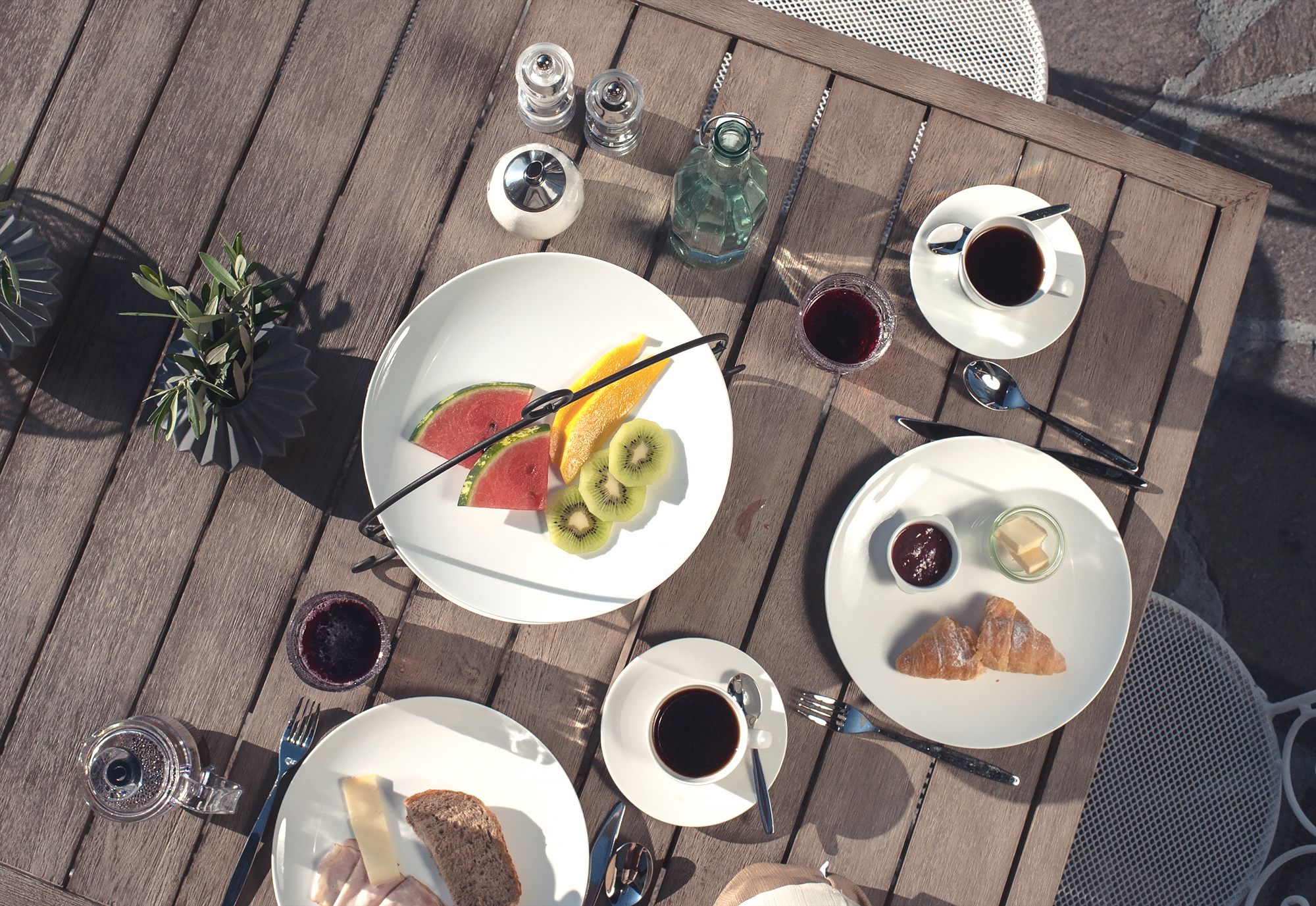 Uma mesa de madeira com diversos itens de pequeno-almoço, incluindo fruta, pão e bebidas.