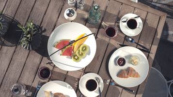 Uma mesa de madeira com diversos itens de pequeno-almoço, incluindo fruta, pão e bebidas.