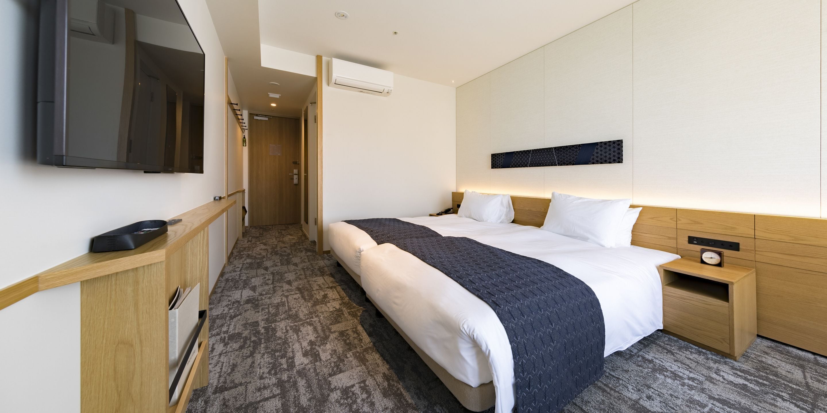 Quarto de hotel com uma cama grande, uma mesa de cabeceira, televisão de tela plana na parede e piso coberto por carpete.
