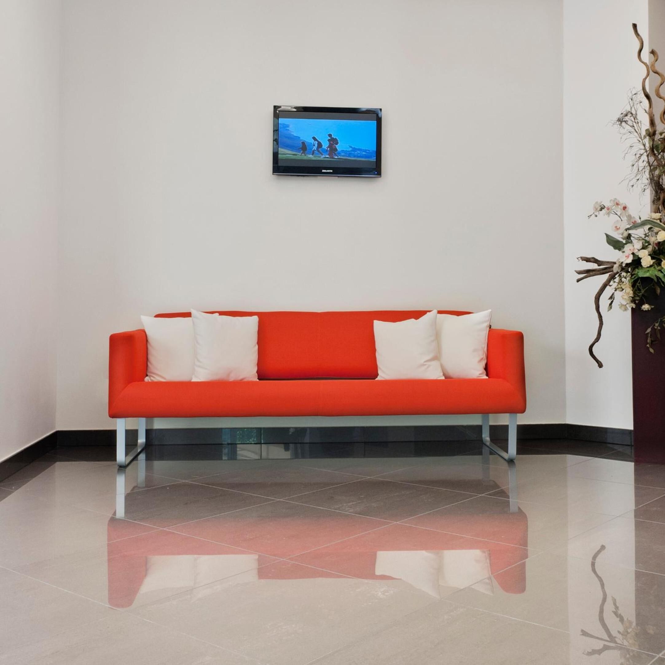 Um hall moderno com um sofá vermelho, uma TV de tela plana na parede e uma planta decorativa.