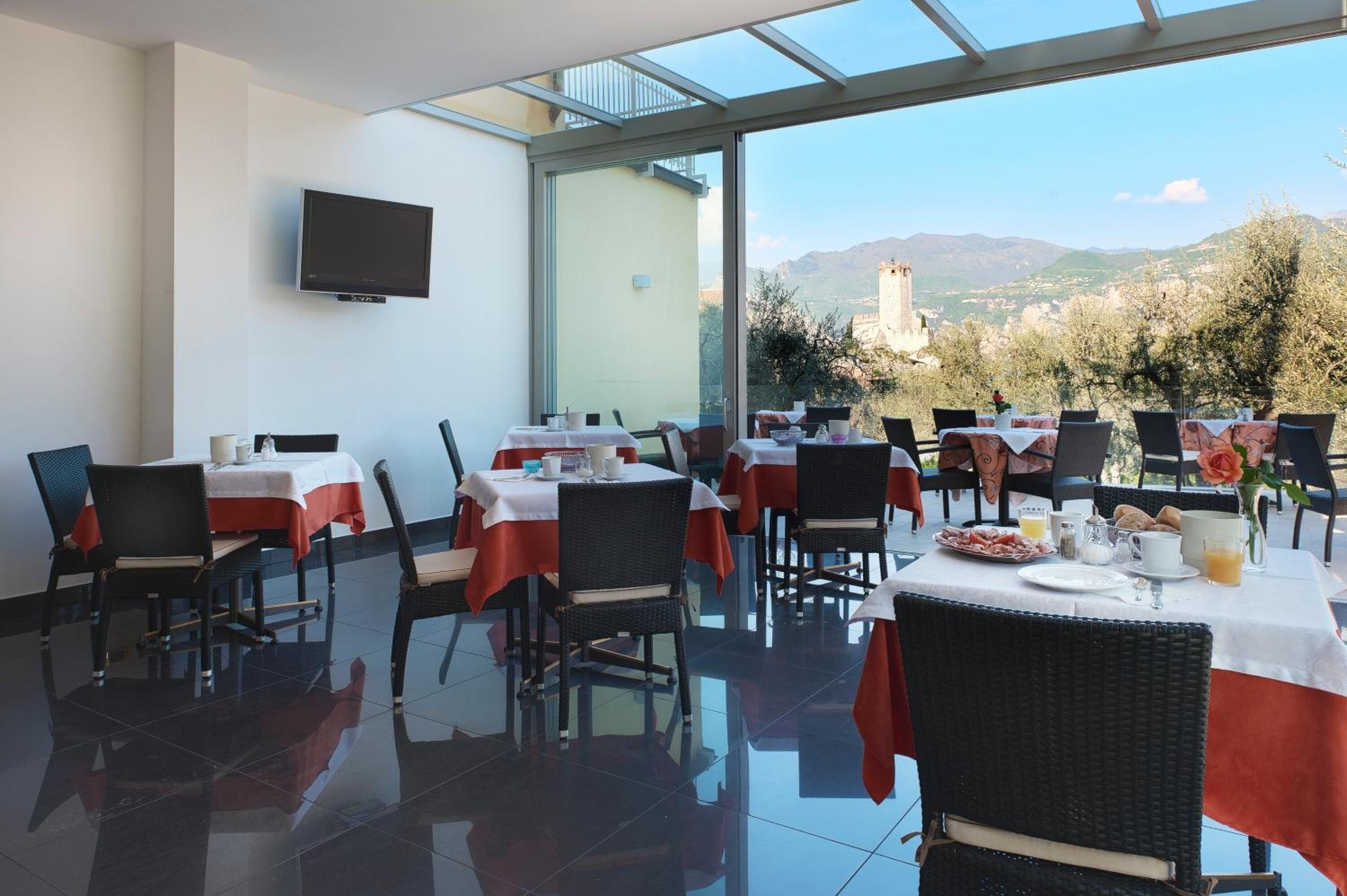 Restaurante com mesas preparadas para refeições, uma televisão na parede e vista para o campo.
