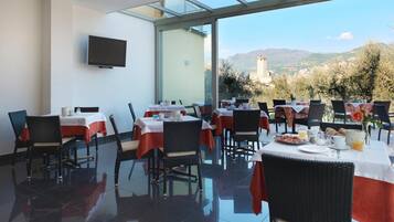 Restaurante com mesas preparadas para refeições, uma televisão na parede e vista para o campo.