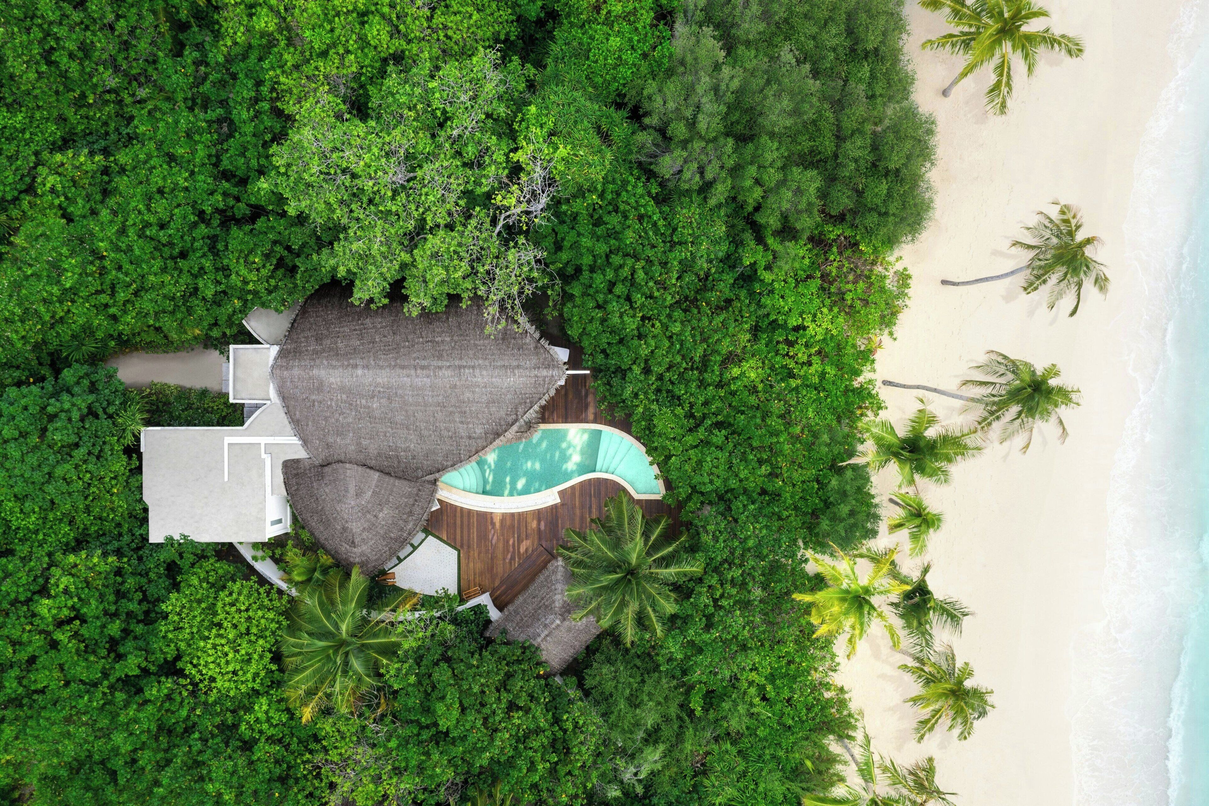 Vista aérea de um resort com piscina, cercado por vegetação exuberante e palmeiras, com vista para uma praia arenosa.