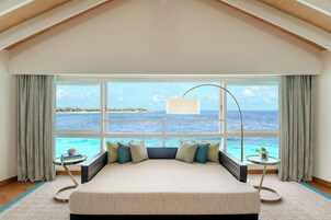 Quarto com cama grande, vista para o oceano e janela com cortinas.