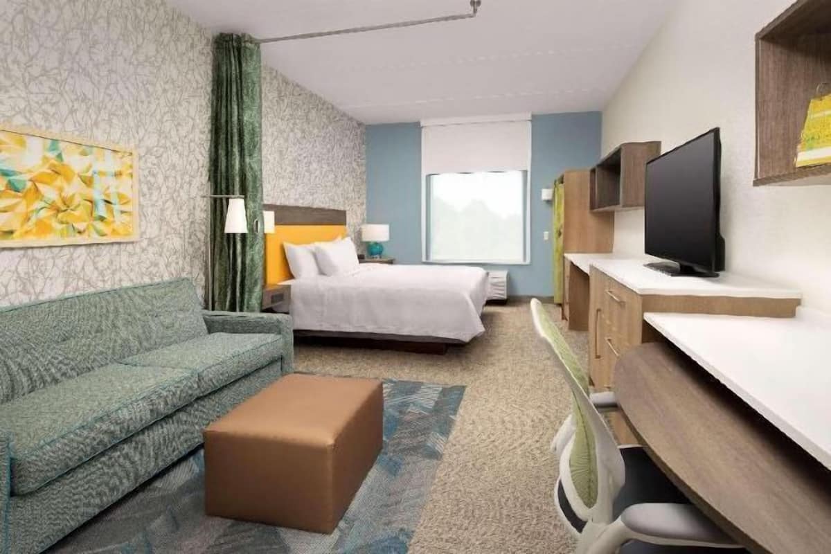 Quarto de hotel com cama, sofá, escrivaninha, televisão e janela.