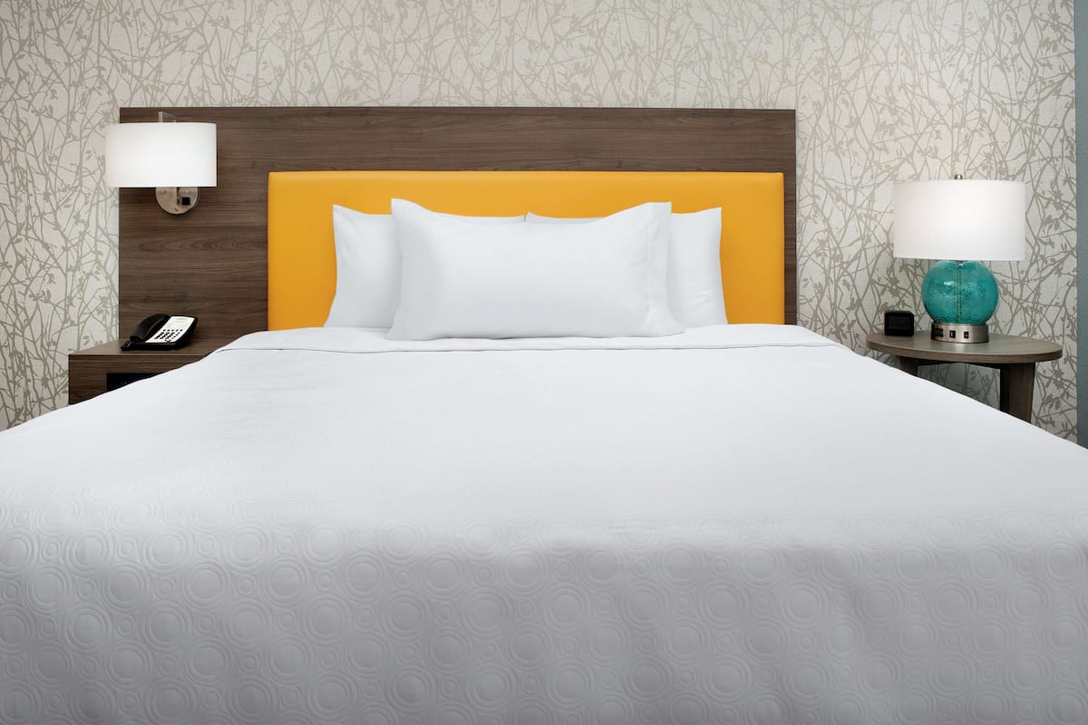 Quarto de hotel com uma cama grande, cabeceira de madeira, mesa de cabeceira com um telefone e uma luminária.
