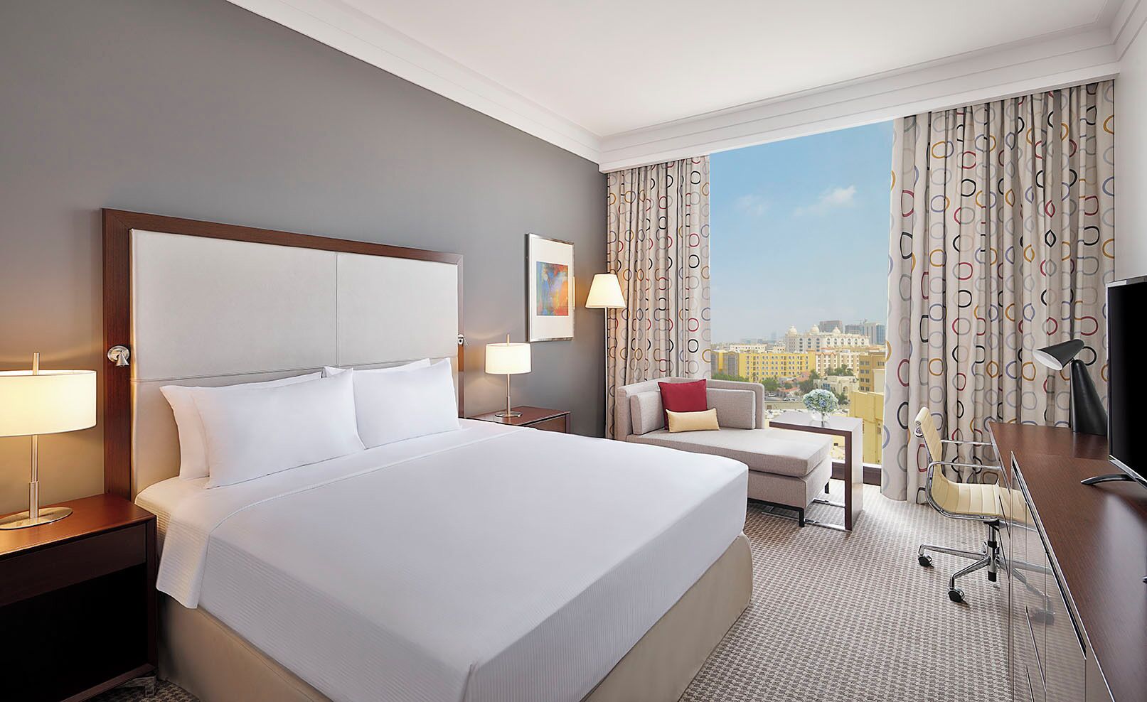 Quarto de hotel com cama grande, sofá, escrivaninha e vista para a cidade.