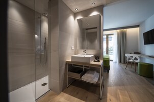 Uma casa de banho moderna com cabine de duche em vidro, um lavatório com espelho em cima e chão em madeira.
