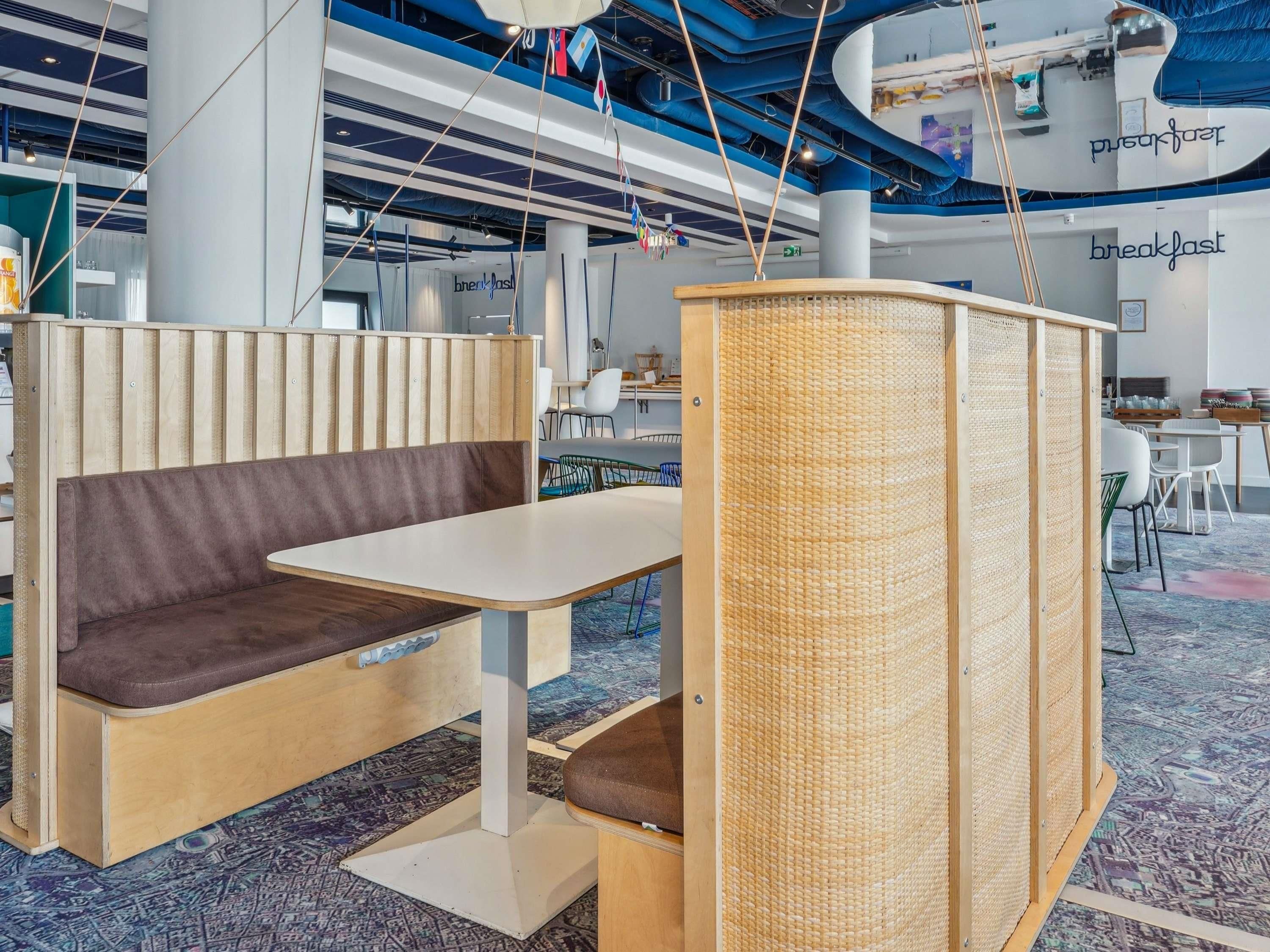 Um espaço de escritório moderno com divisória de madeira, uma mesa branca e um banco acolchoado castanho.