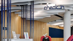 Uma área de recepção moderna com balcão de check-in, cadeiras vermelhas e um vaso decorativo.