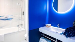 Casa de banho moderna com cabine de duche em vidro, lavatório branco e parede azul decorativa, e espelho redondo com iluminação em volta.