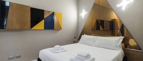 Quarto moderno com cama, roupa de cama branca e uma obra de arte geométrica na parede.