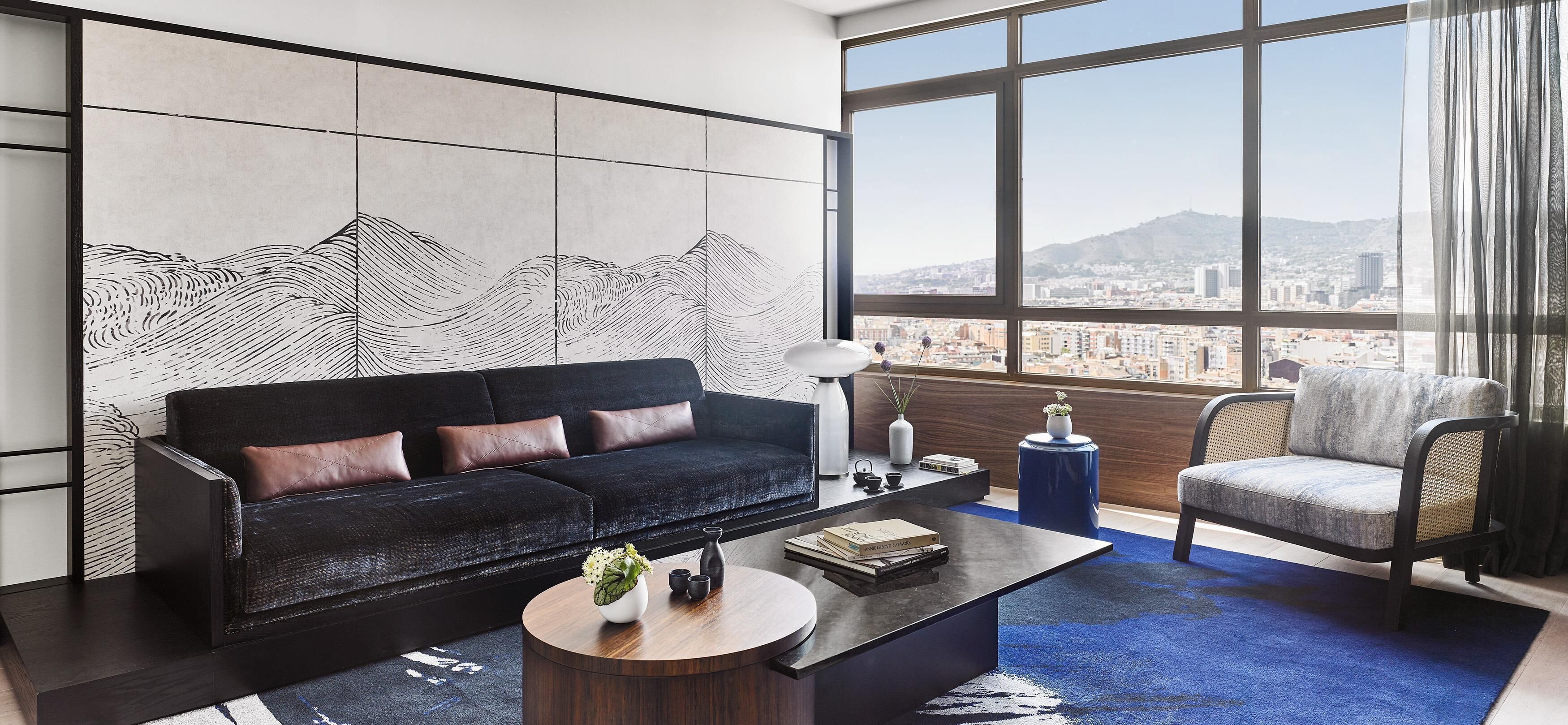 Sala de estar moderna com um sofá preto, uma mesa de centro redonda e vista para um horizonte urbano através de grandes janelas.