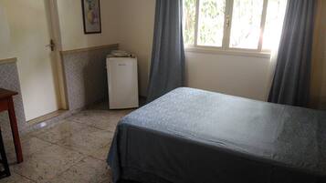 Quarto pequeno com cama, escrivaninha e geladeira.
