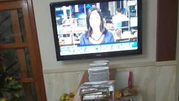 Uma mesa de buffet com diversos alimentos e uma televisão fixada na parede.