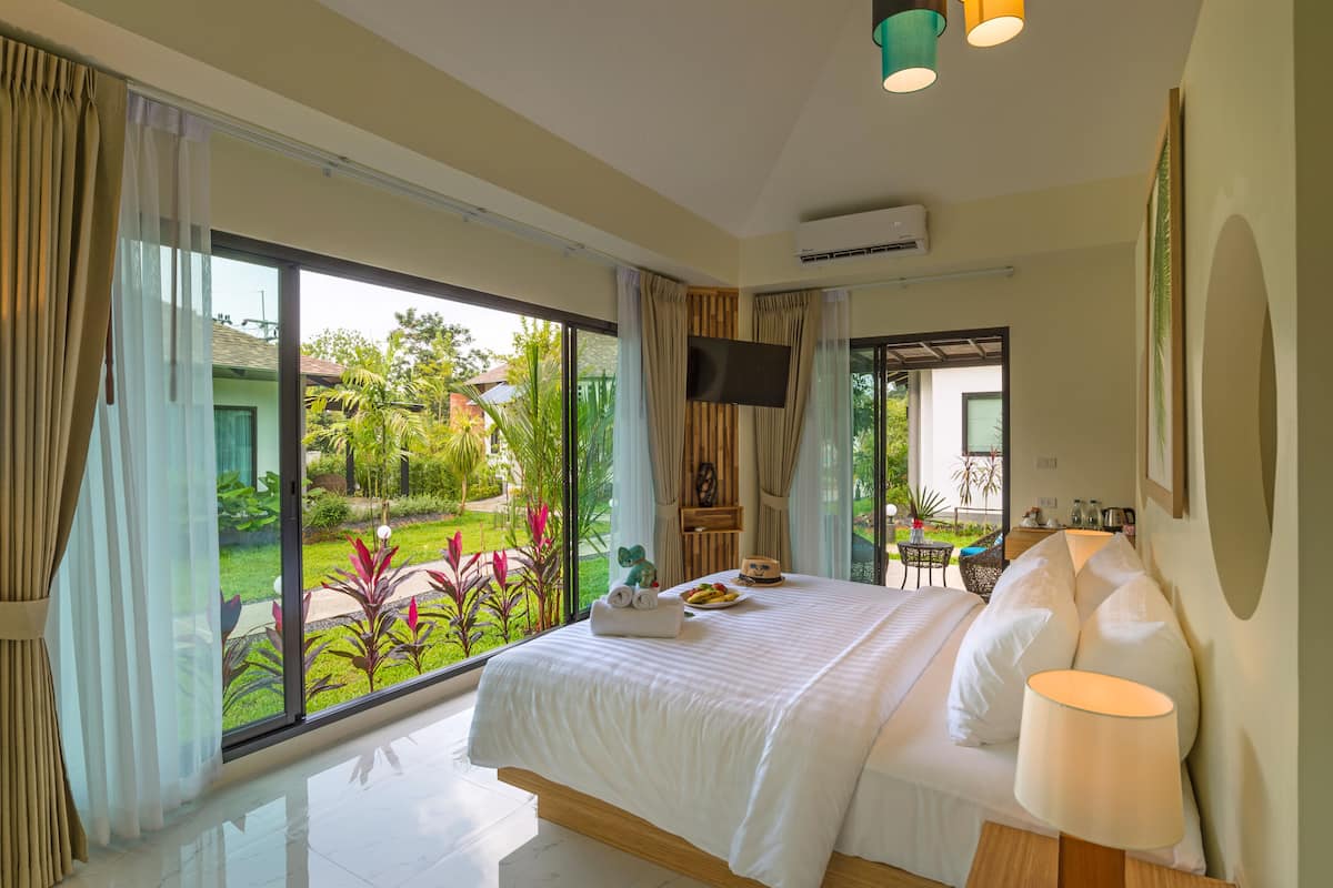 Quarto espaçoso com uma cama grande, TV montada na parede e vista para um jardim exuberante.
