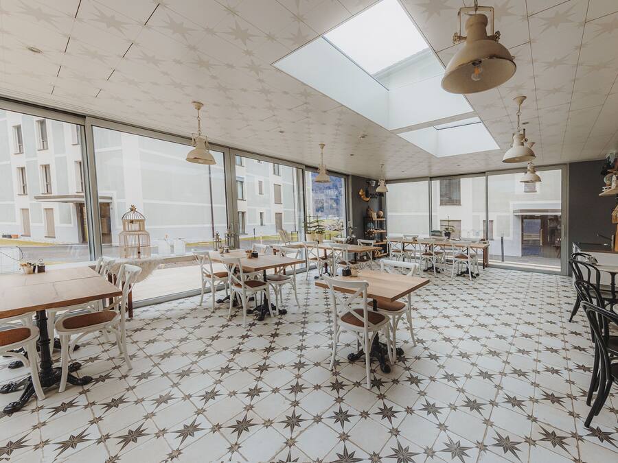 Uma ampla sala de jantar com várias mesas e cadeiras, grandes janelas com vista para a cidade e um design de teto moderno com claraboias.