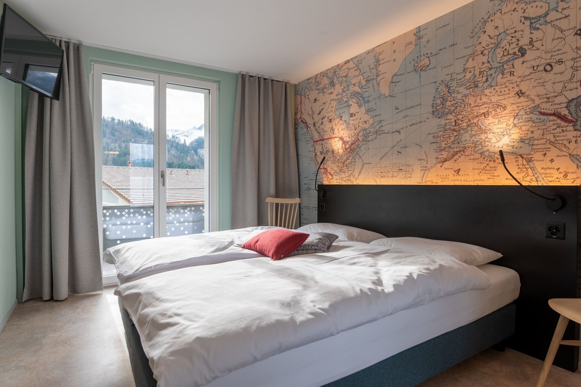 Quarto com cama grande, mapa na parede, televisão e vista para uma montanha.
