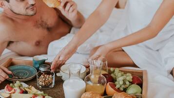 Um casal na cama com café da manhã em uma bandeja, incluindo frutas, croissants e suco.