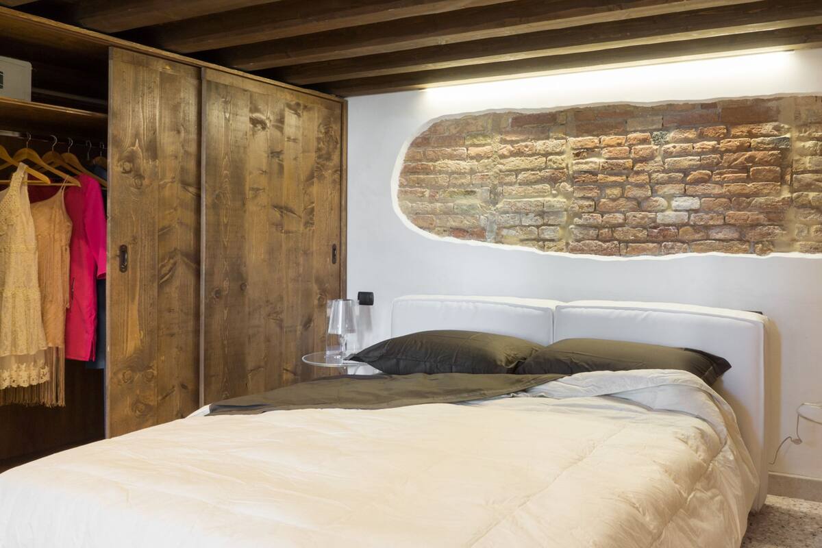 Quarto com cama, guarda-roupa de madeira e parede de tijolos.