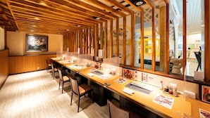 Interior de restaurante com painéis de madeira, um balcão comprido com cadeiras e vista através de um divisório de vidro.